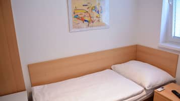 Uma cama de solteiro com cabeceira de madeira, uma mesa de cabeceira com controle remoto e uma janela com persianas.