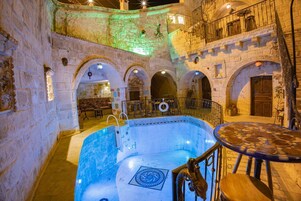 Um edifício histórico com piscina, arcos de pedra e varanda com grades de metal.