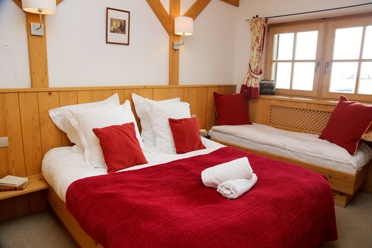 Quarto de hotel com cabeceira de madeira, manta vermelha e colcha branca.