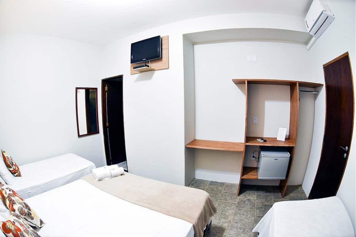 Quarto de hotel com duas camas, televisão fixada na parede, secretária com cadeira e um frigorífico pequeno.