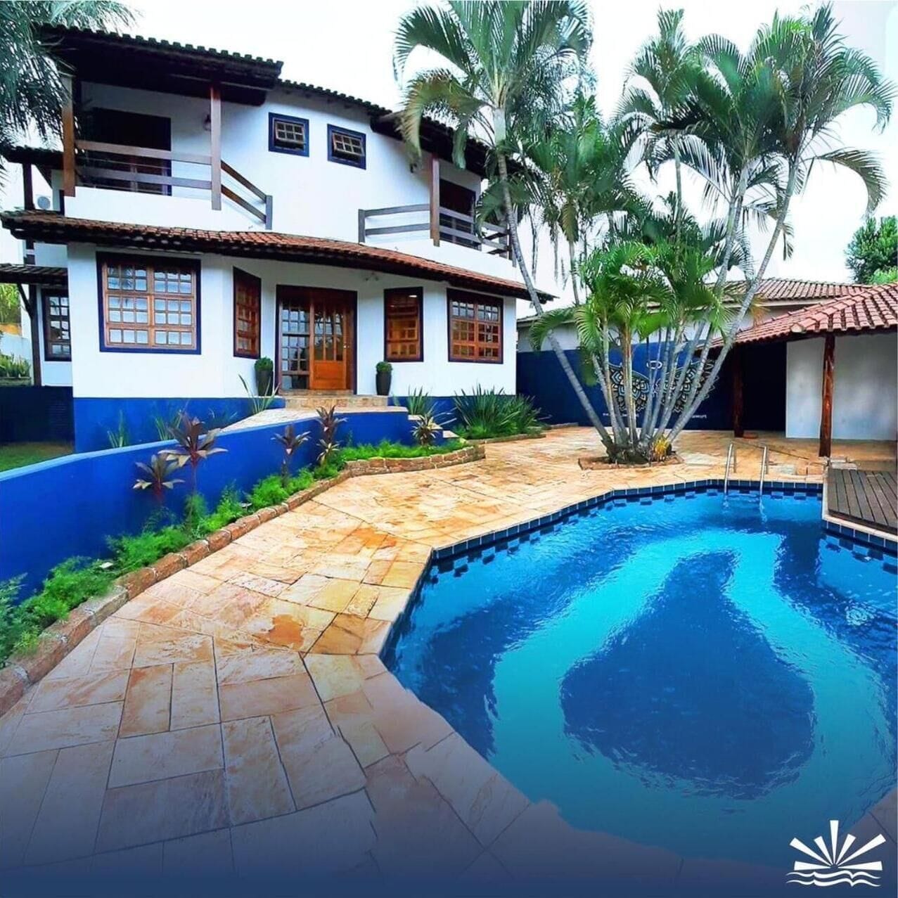 Uma casa de dois andares com piscina, cercada por palmeiras e fachada azul e branca.