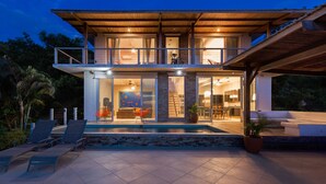 Uma casa moderna de dois andares com piscina, área de estar ao ar livre e uma grande porta de vidro que dá para o interior.