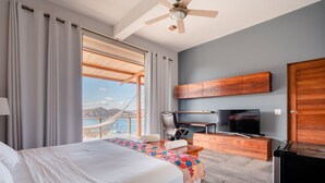 Quarto de hotel com cama, escrivaninha, televisão e vista para o mar.