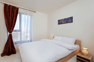 Um quarto com cama, mesa de cabeceira, uma obra de arte na parede e janela com cortinas.