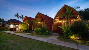 Uma fileira de cabanas de madeira com telhados inclinados, cercada por vegetação exuberante e palmeiras.