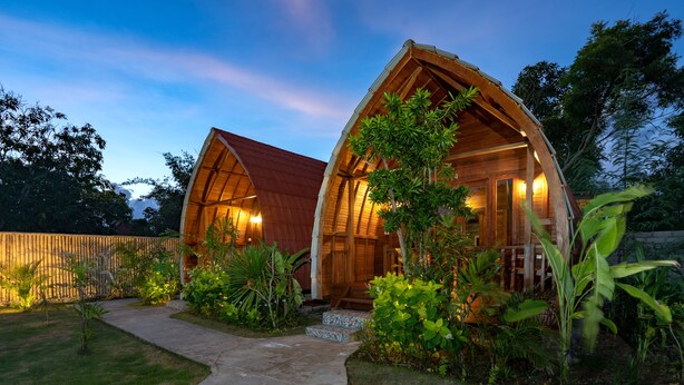 Uma cabana de madeira com telhado curvo e um caminho de concreto que leva à entrada.