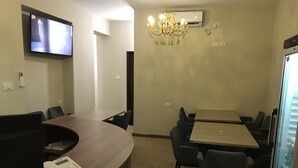 Uma sala de conferências com uma mesa comprida, cadeiras, um telefone, uma TV fixada na parede e um lustre.