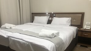 Cama bem arrumada com roupa de cama e toalhas brancas, cabeceira de madeira e mesa de cabeceira com telefone.