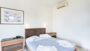 Uma cama bem arrumada com toalhas brancas, cabeceira de madeira e mesa de cabeceira com abajur.
