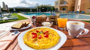 Um ambiente de café da manhã com omelete, torradas, frutas e café em uma mesa de madeira à beira da piscina.