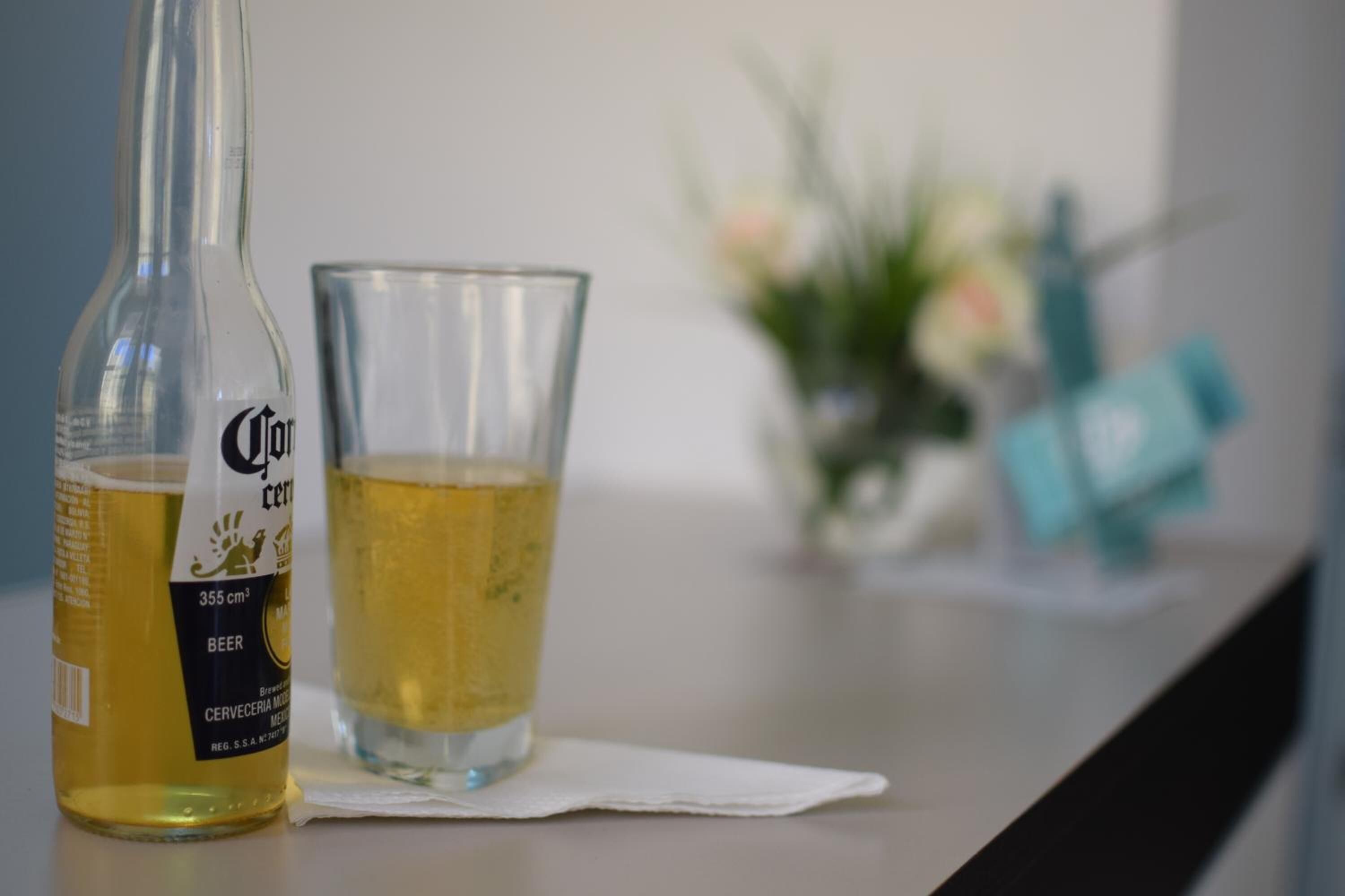 Uma garrafa de cerveja e um copo sobre uma mesa com guardanapo branco.