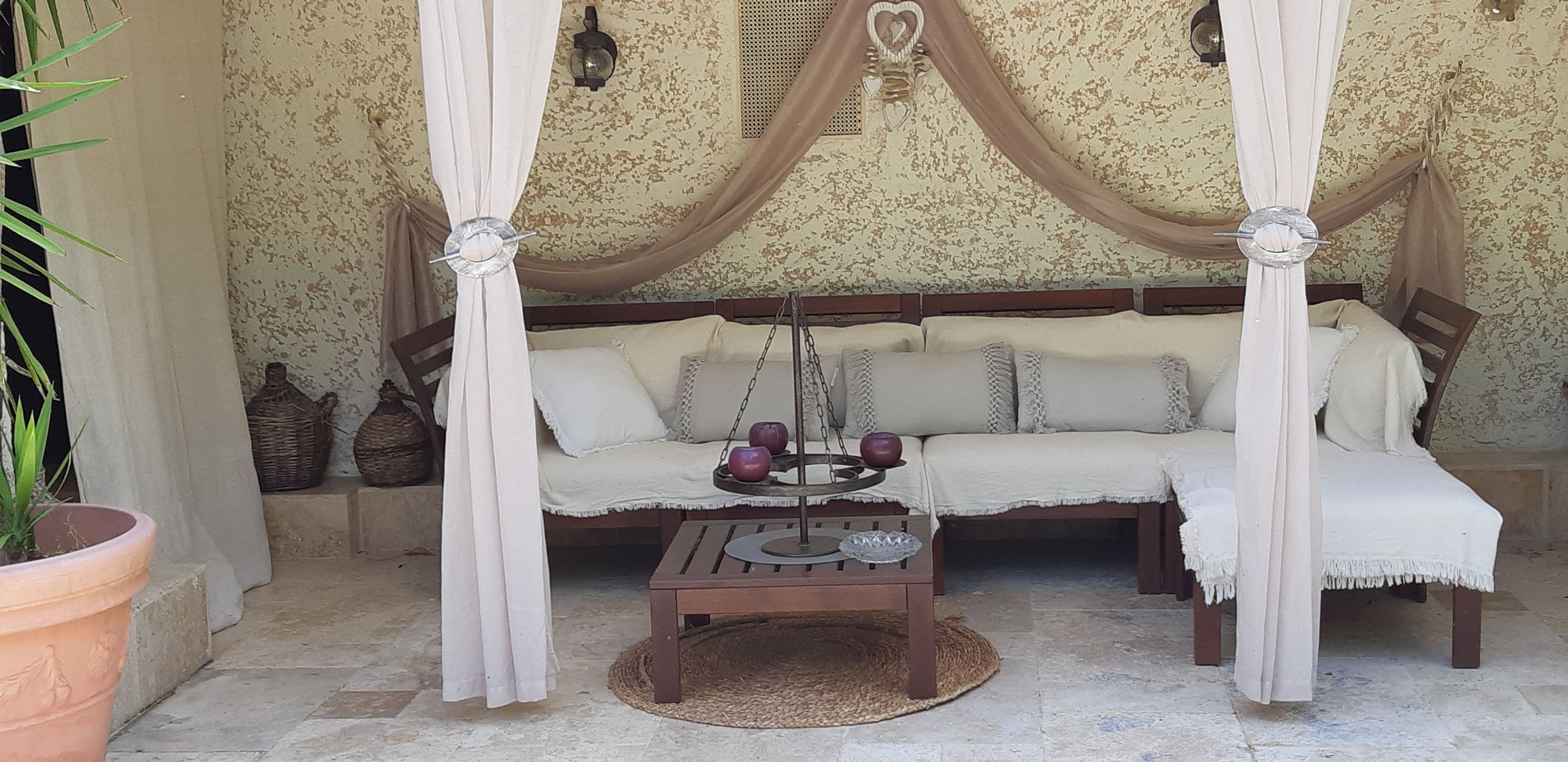 Uma cama com dossel e cortina, um tapete tecido, uma mesinha e objetos decorativos.