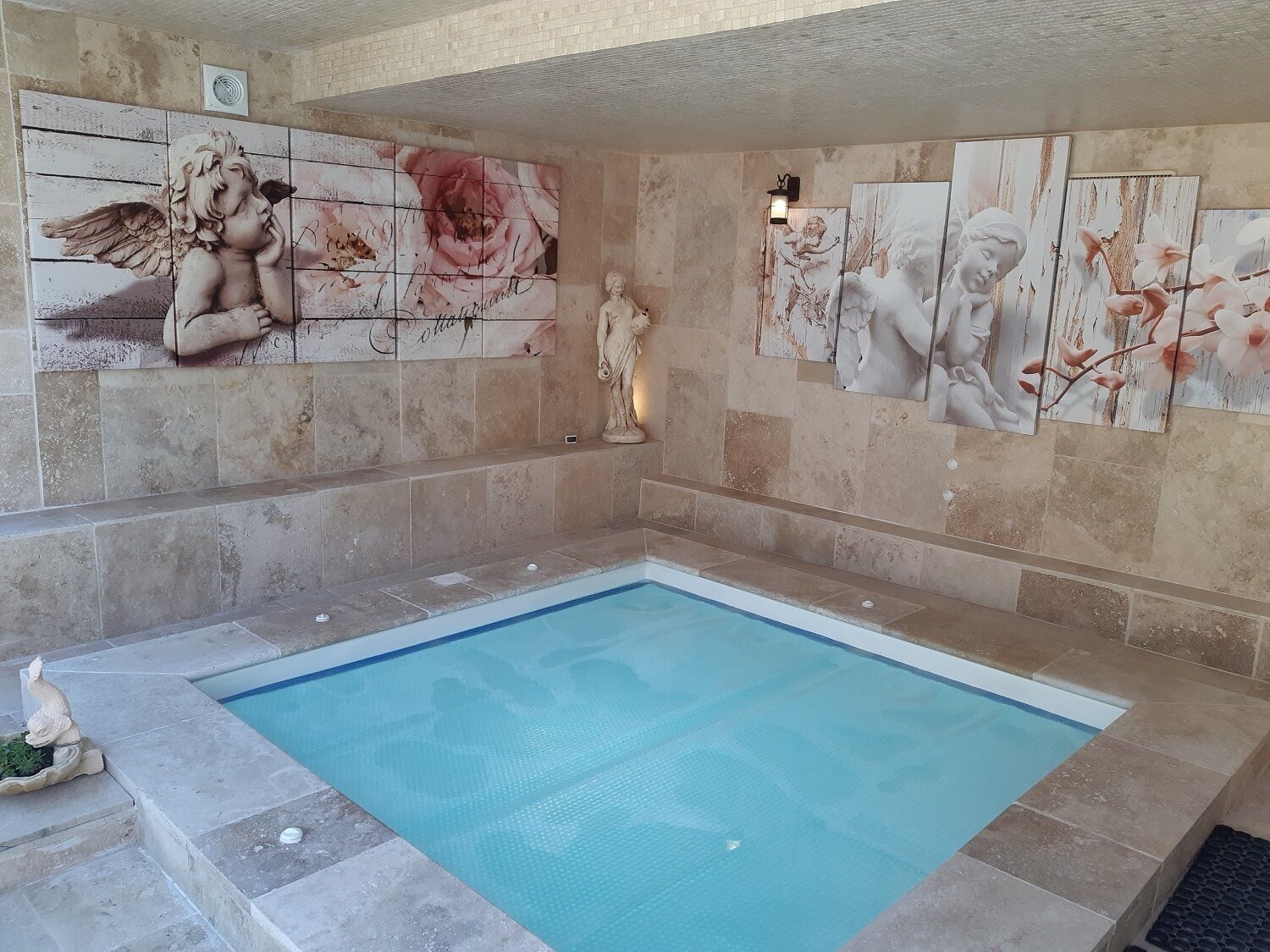 Piscina com muro de pedra e painéis decorativos, incluindo um querubim e motivos florais.