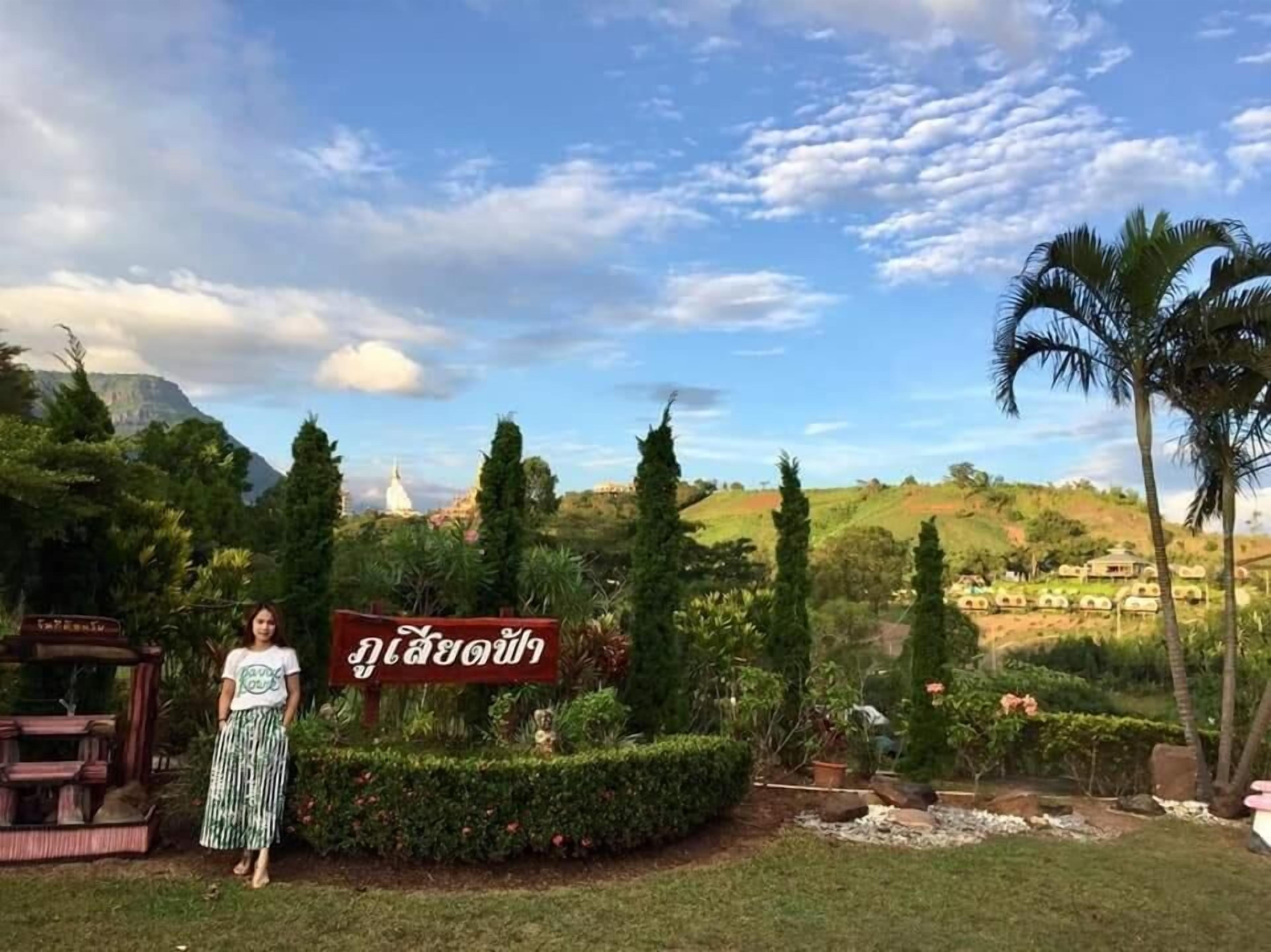 Mulher em frente a um letreiro com vista para uma colina e um templo ao fundo.