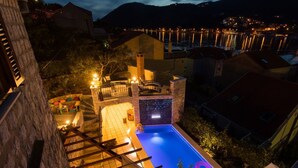 Piscina no terraço com vista para a cidade, paredes de pedra e iluminação externa.