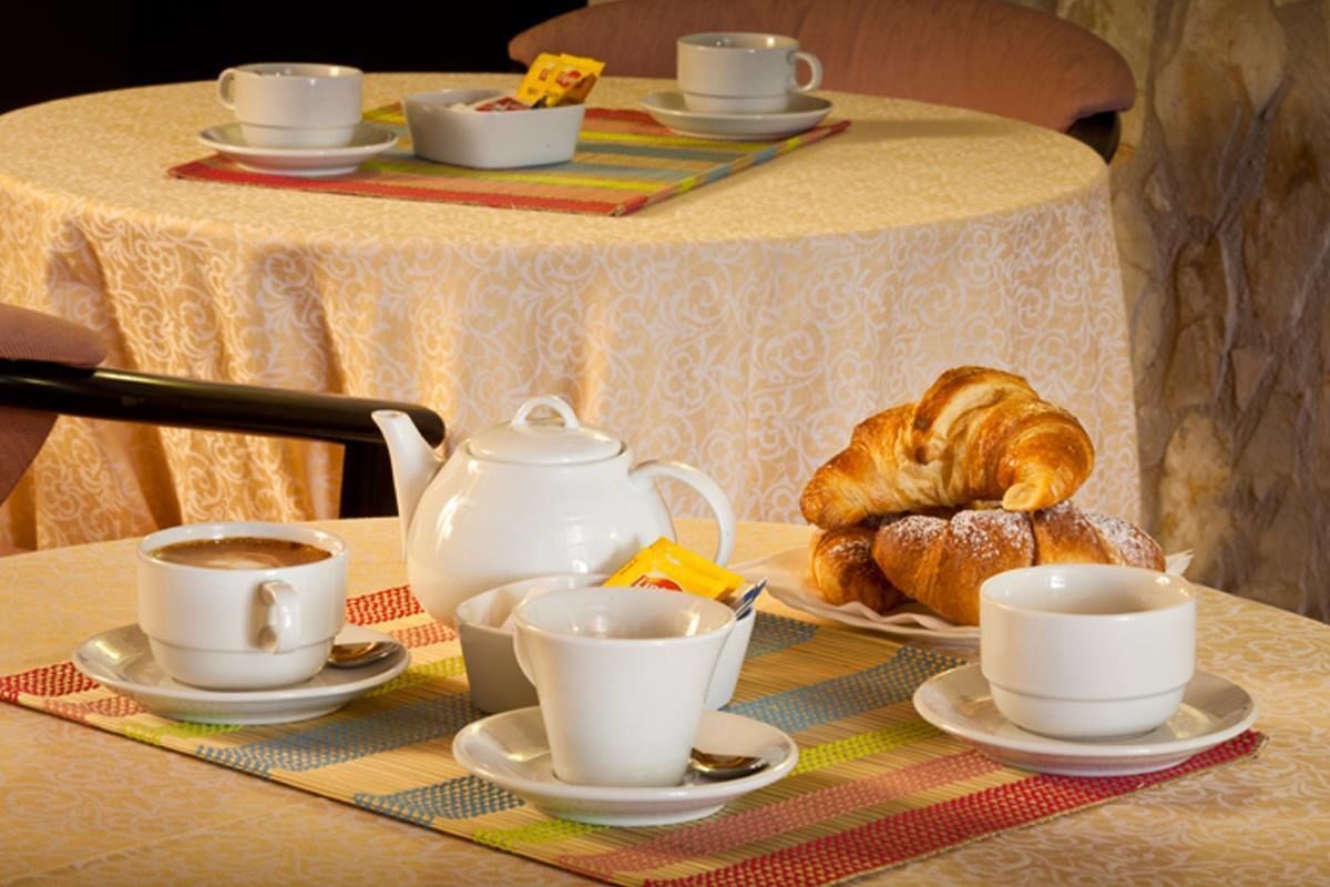 Mesa posta para o café da manhã, com café, croissants e chá, sobre uma toalha de mesa estampada.
