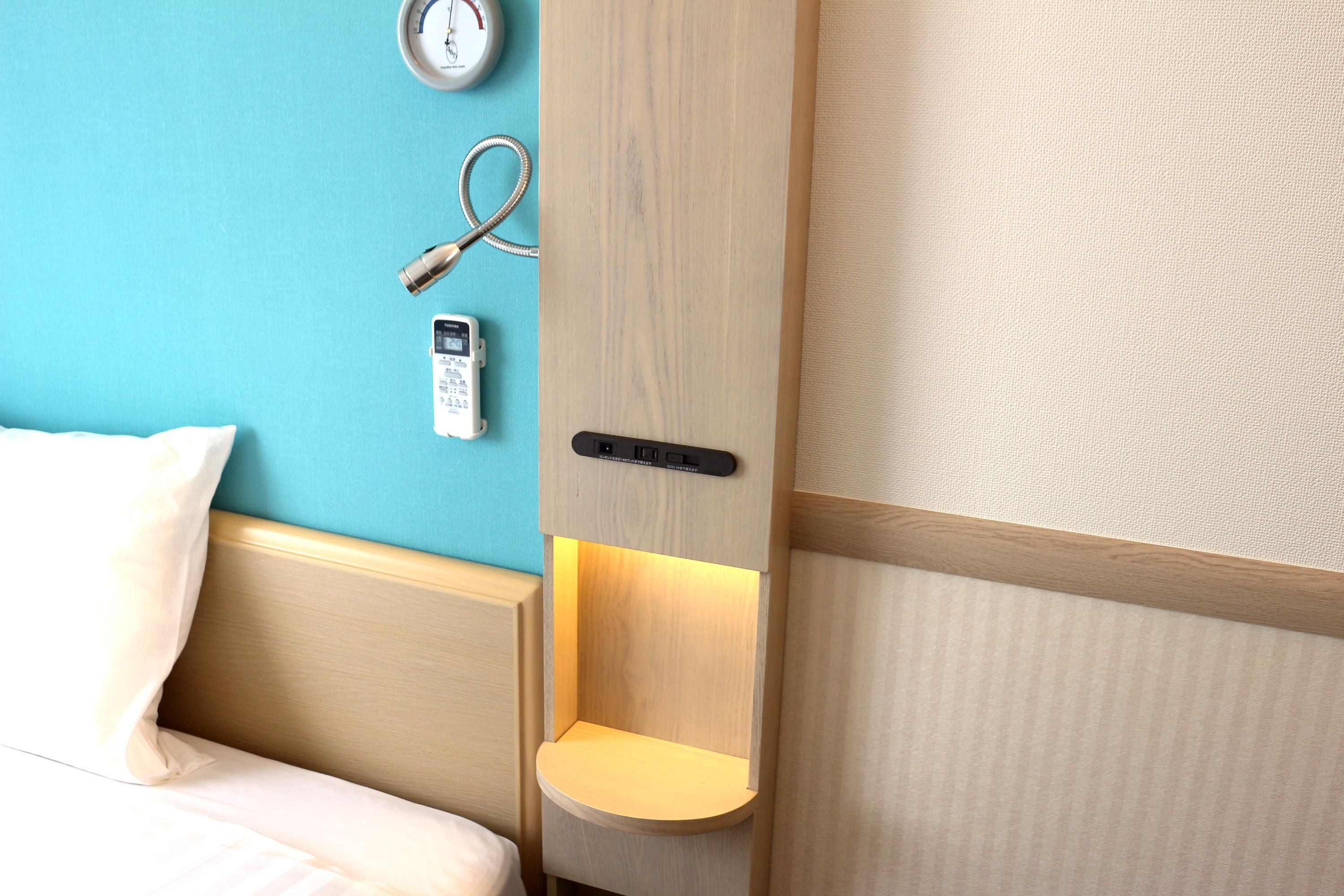 Quarto de hotel com uma cama, mesa de cabeceira com abajur, relógio de parede e telefone.