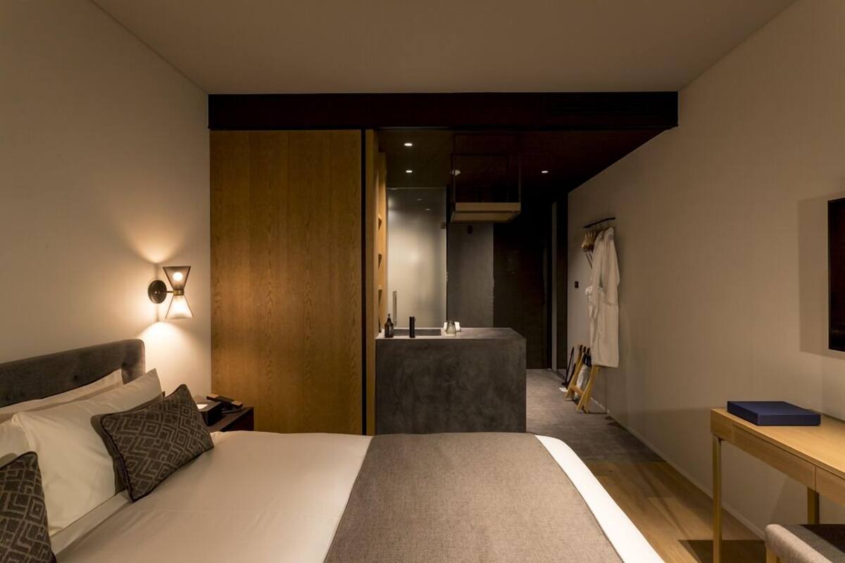 Quarto de hotel moderno com cama grande, mesa de cabeceira e guarda-roupa de madeira.