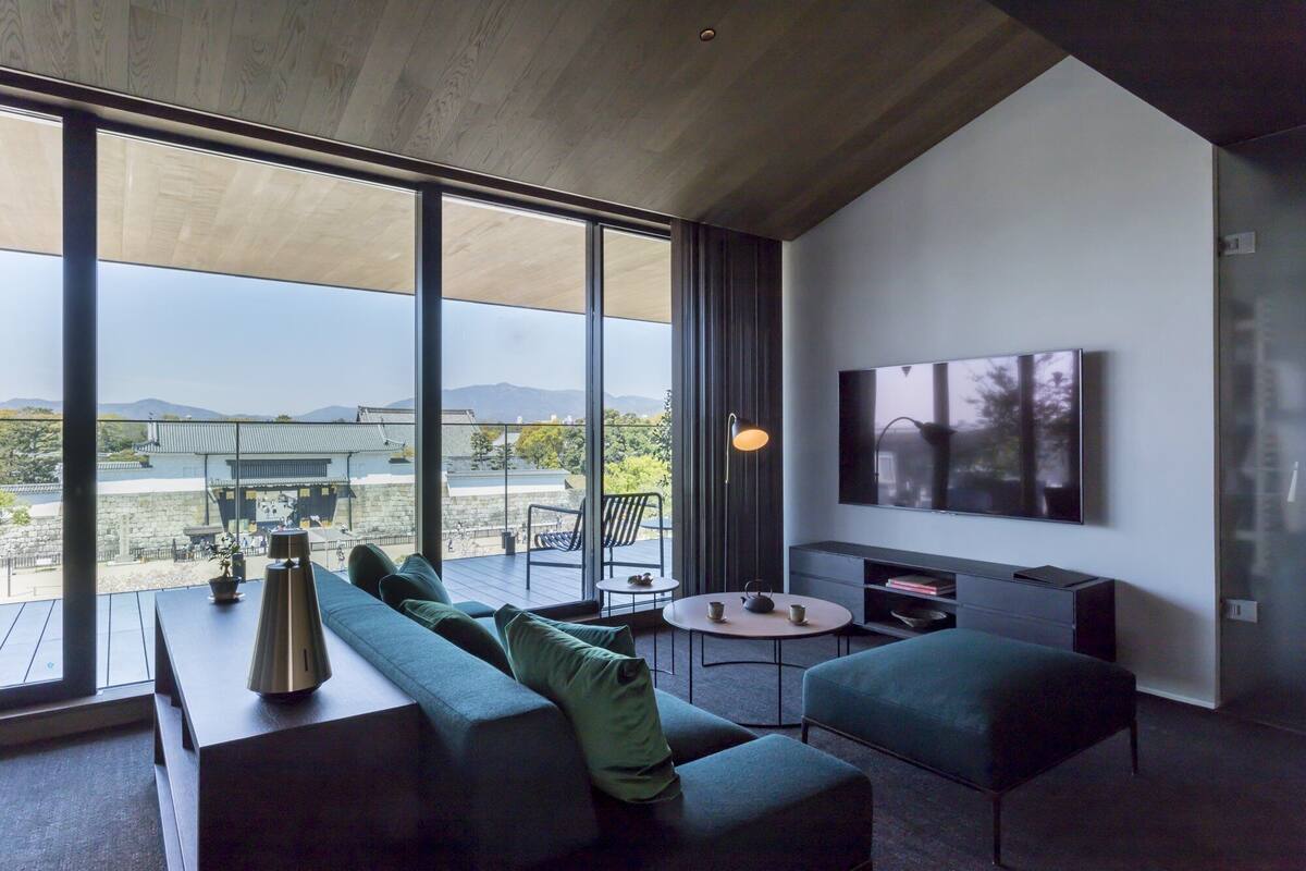 Uma sala de estar moderna com uma janela ampla, uma TV de tela plana, um sofá, uma mesa de centro e uma lareira.