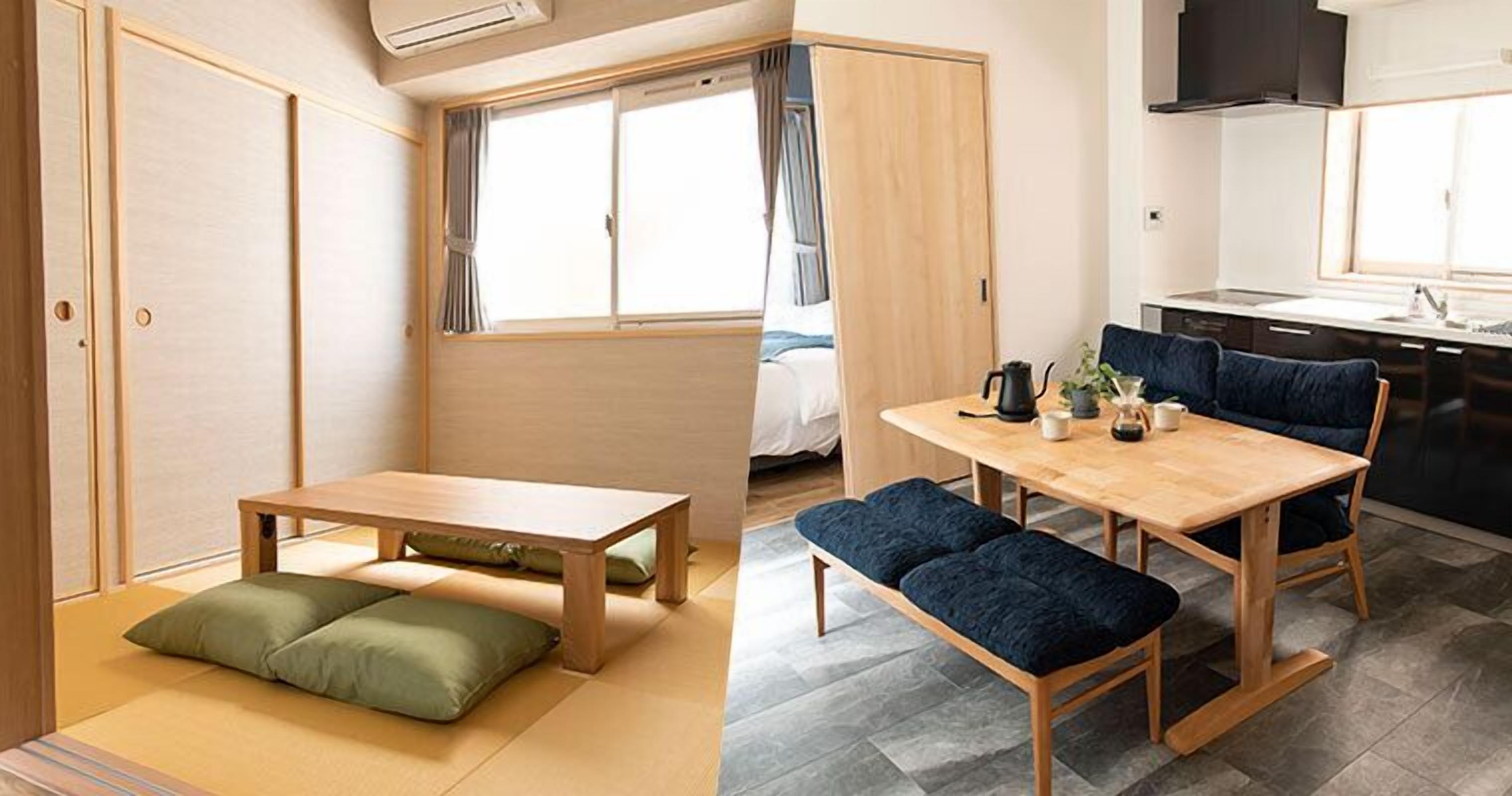 Quarto com mesa de madeira, bancos, cama, janela e cozinha.