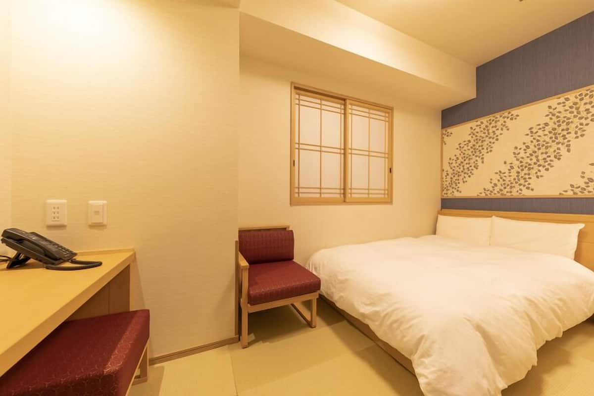 Quarto de hotel com cama, escrivaninha com telefone, cadeira, janela e painel decorativo na parede.
