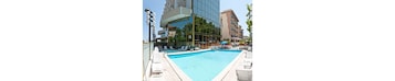 Piscina com espreguiçadeiras e guarda-sóis, cercada por edifícios modernos.