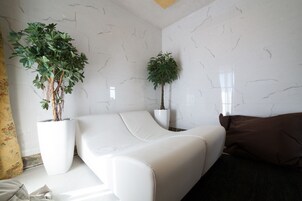Quarto moderno com um sofá branco, duas plantas grandes em vasos e uma almofada marrom.