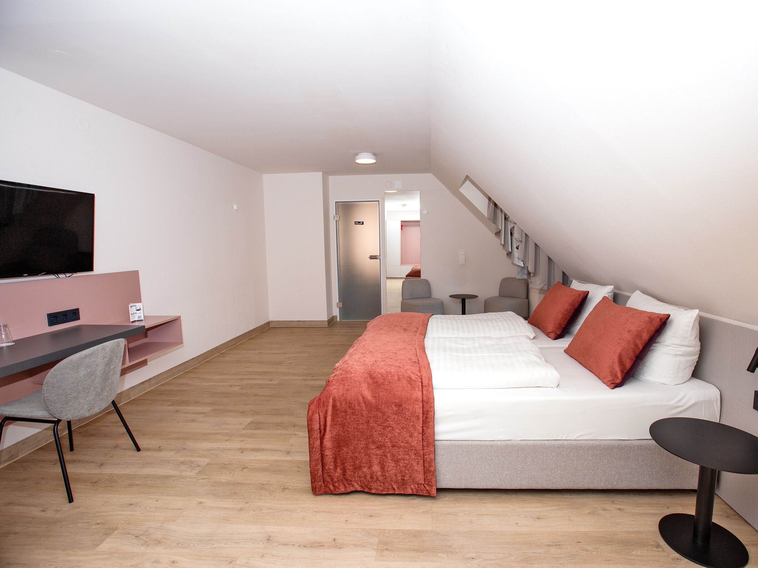 Quarto moderno com cama, escrivaninha e televisão.