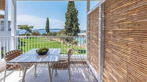 Área externa coberta com mesa e cadeiras, vista para o mar e um painel de bambu.