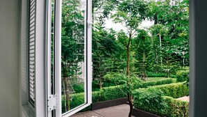 Visão através de uma porta de vidro para um jardim bem cuidado, com sebes e árvores podadas.