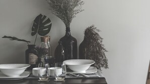 Uma mesa de jantar com pratos brancos, copos e um vaso com plantas secas.