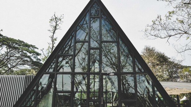 Um edifício de vidro triangular com design moderno, rodeado por árvores.
