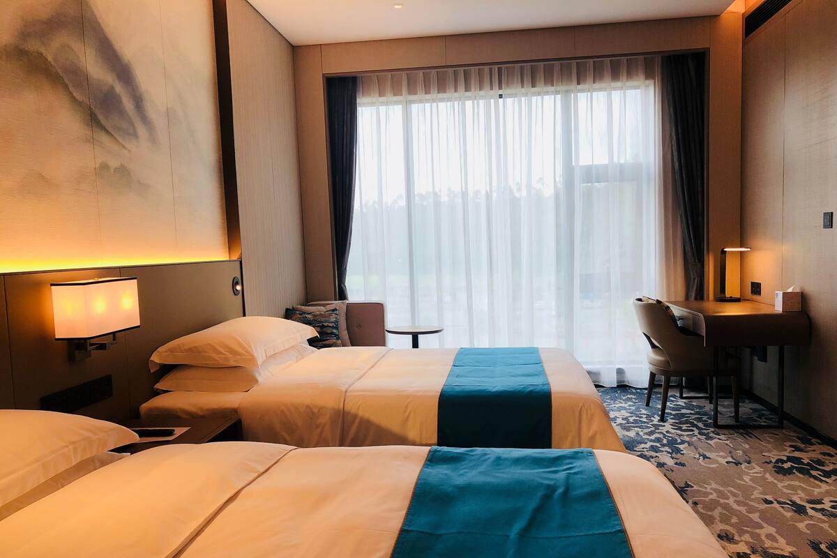 Quarto de hotel com duas camas, uma escrivaninha e uma cadeira.