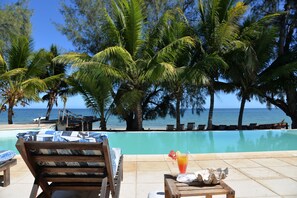 Área à beira da piscina com espreguiçadeiras, uma mesa com bebida e vista para o mar.