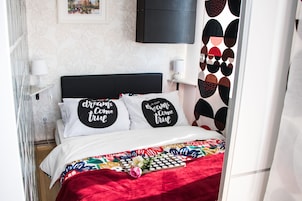 Cama bem arrumada com um cobertor colorido e duas almofadas com frases motivacionais.