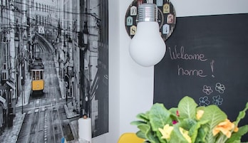 Pintura em preto e branco de uma paisagem urbana, um quadro-negro com a mensagem 'Welcome home!' e uma lâmpada na parede.