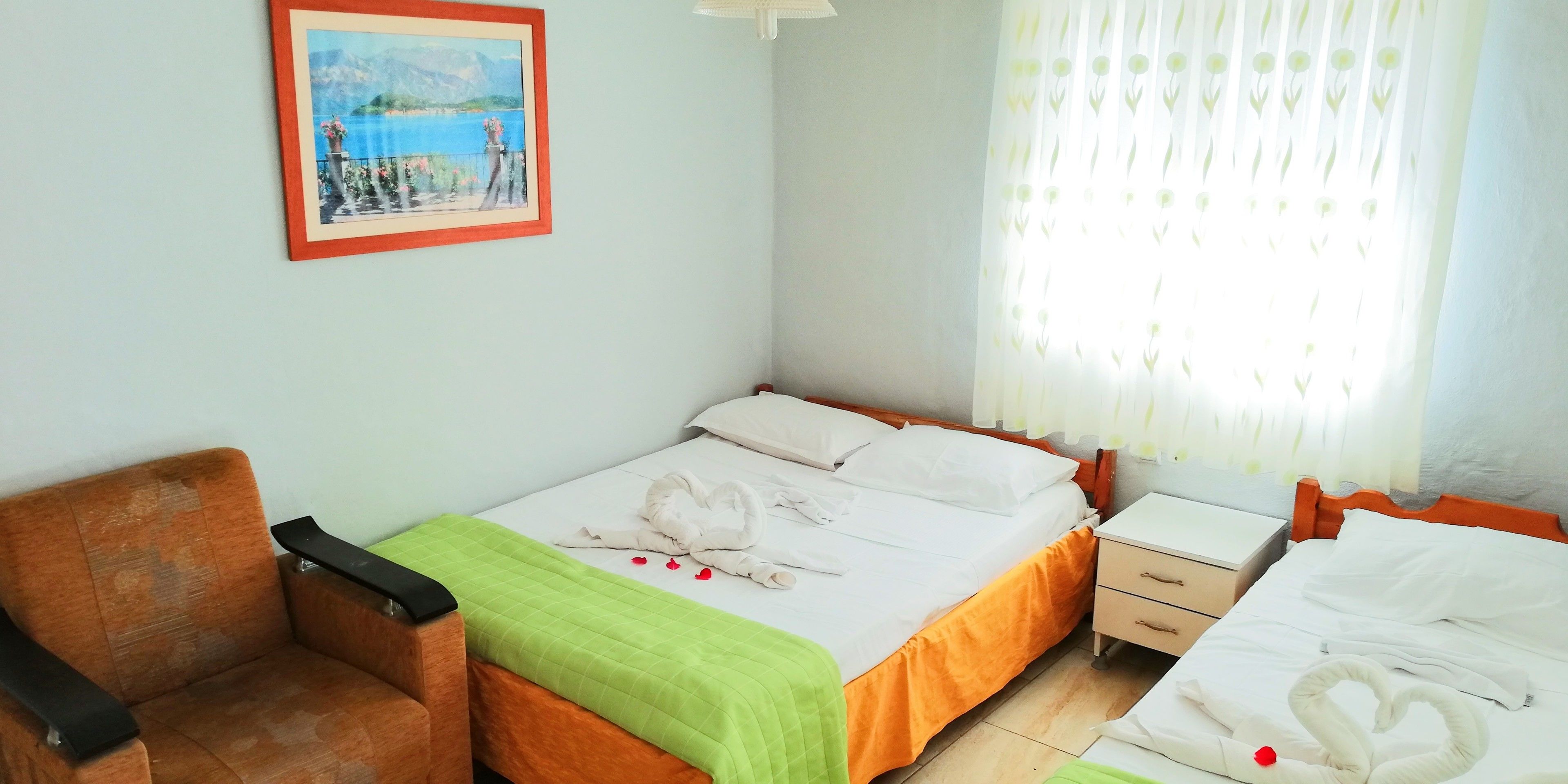 Quarto de hotel com cama, uma cadeira, mesa de cabeceira e janela com cortinas.