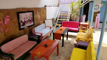 Uma área de estar ao ar livre aconchegante com diversos móveis coloridos, incluindo um sofá rosa, uma cadeira amarela e uma mesa vermelha.