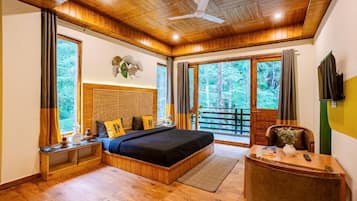 Quarto com teto de madeira, cama, escrivaninha e uma grande janela com vista para árvores.