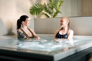 Duas mulheres em uma banheira de hidromassagem, com uma planta ao fundo.