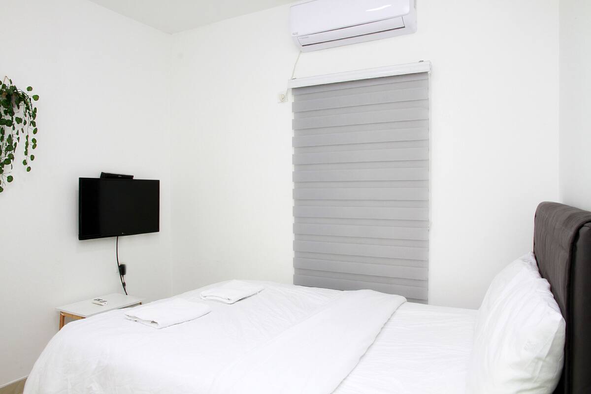 Quarto de hotel com uma cama, televisão, mesa de cabeceira e ar condicionado.