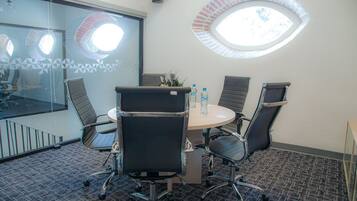 Uma sala de conferências com uma mesa redonda, seis cadeiras e um painel de vidro com padrão geométrico.