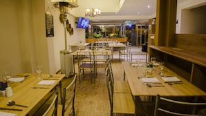 Um restaurante com várias mesas e cadeiras, uma tela de televisão e um candelabro.