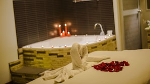 Quarto de hotel com banheira, velas e pétalas de rosa na cama.