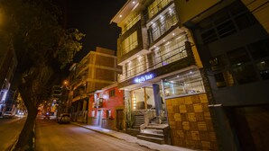 Um hotel com vários andares e fachada moderna, com uma escadaria visível que leva à entrada, e uma rua bem iluminada.