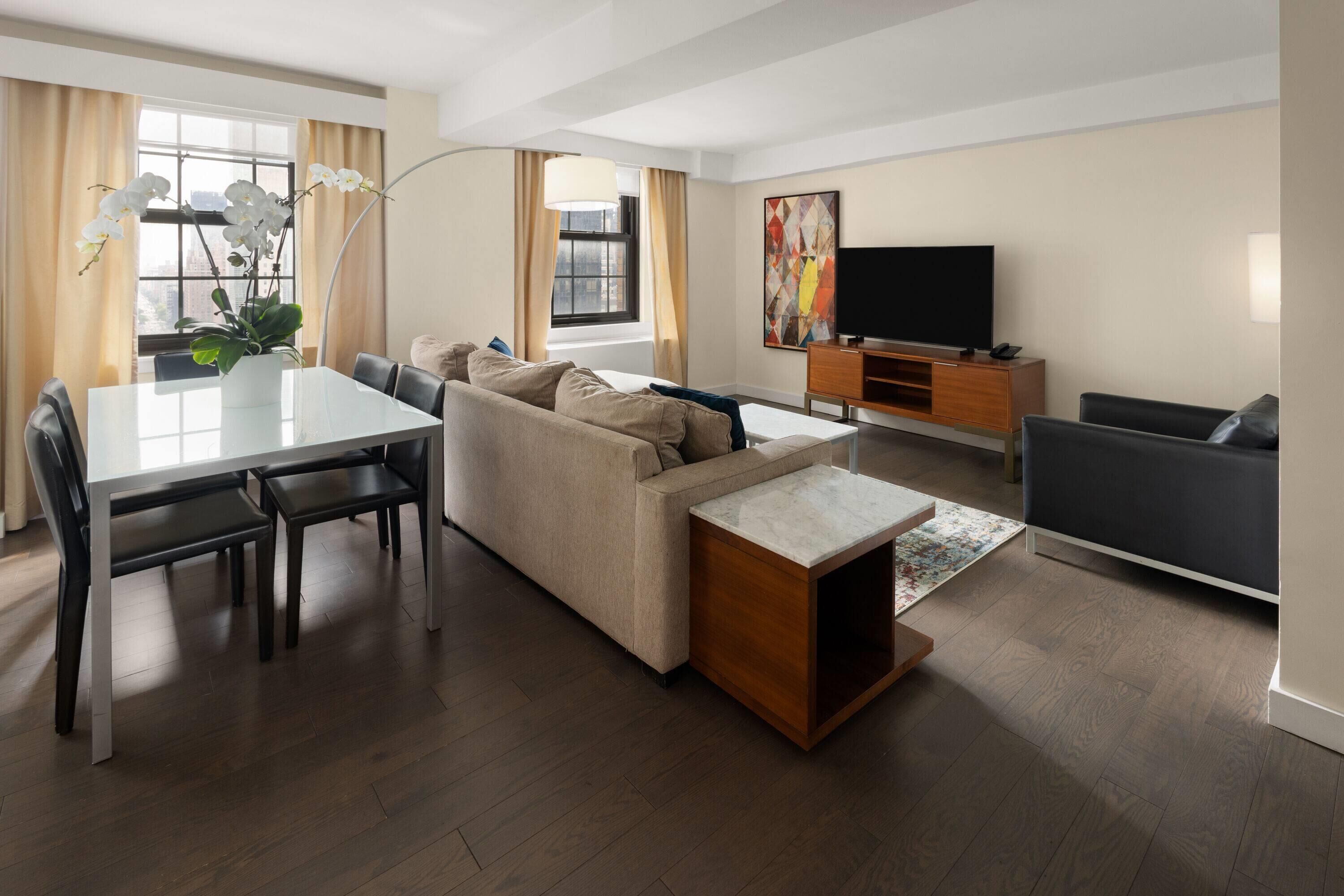 Uma sala de estar moderna com sofá, mesa de jantar, cadeiras, televisão e uma planta.