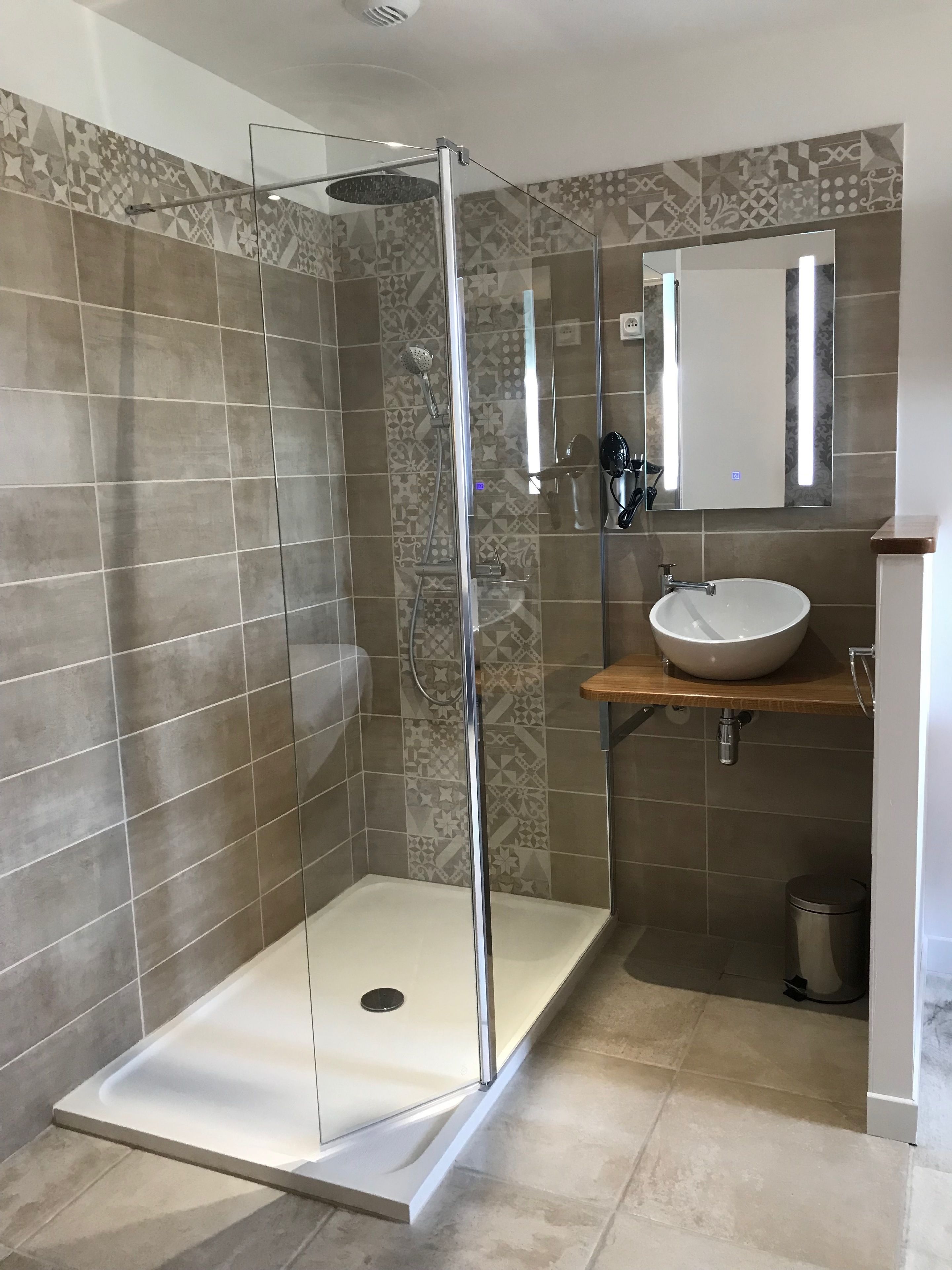 Uma casa de banho moderna com chuveiro envidraçado, lavatório branco e painel de azulejos estampados.