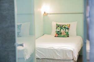 Cama bem arrumada com travesseiro floral e luminária na parede.