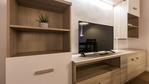 Uma sala de estar moderna com uma TV de tela plana presa a um móvel de madeira, uma pequena planta em vaso e um controle remoto sobre o suporte da TV.