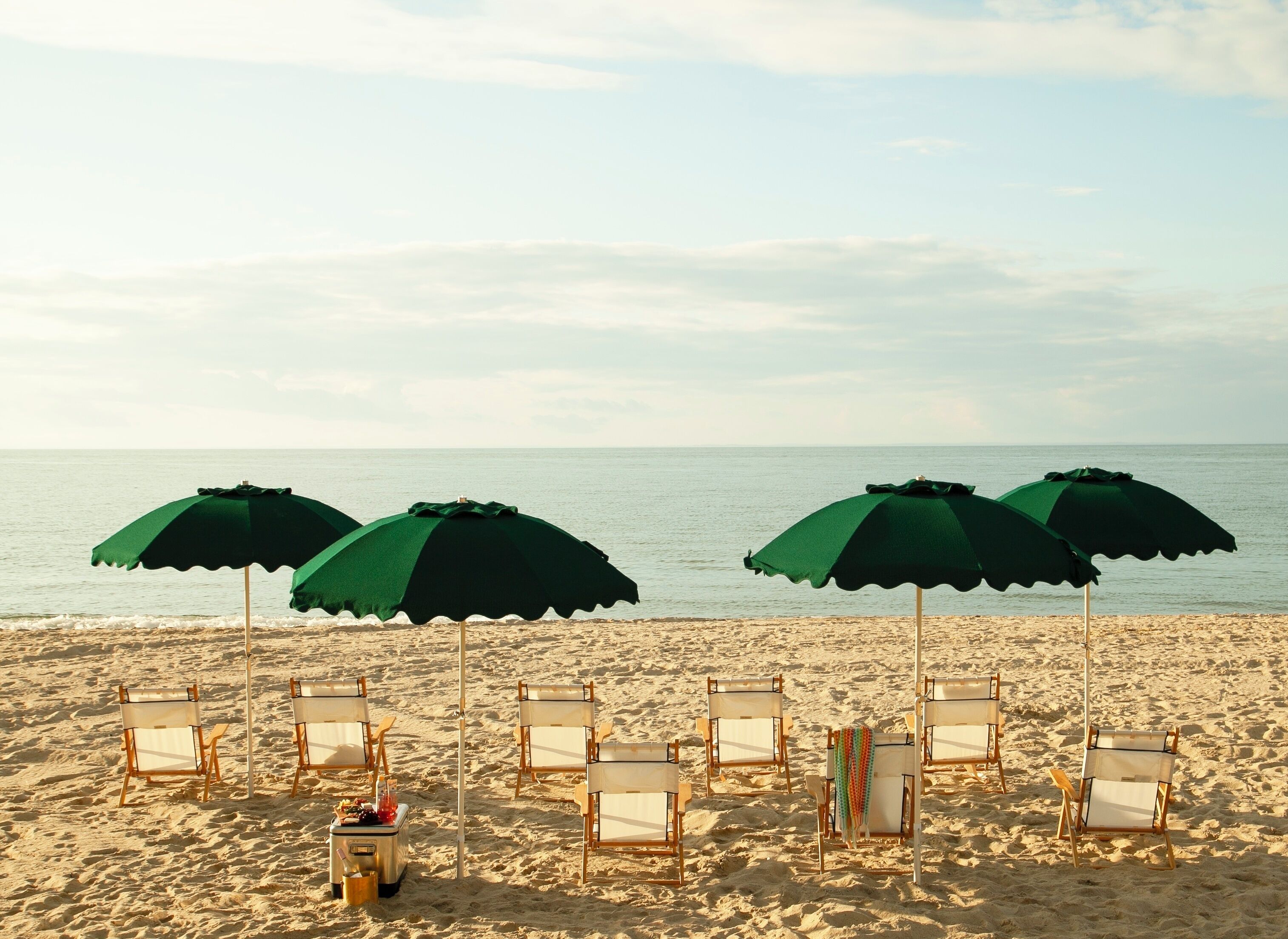 Uma praia com fileiras de espreguiçadeiras e guarda-sóis verdes, dispostas para banho de sol.